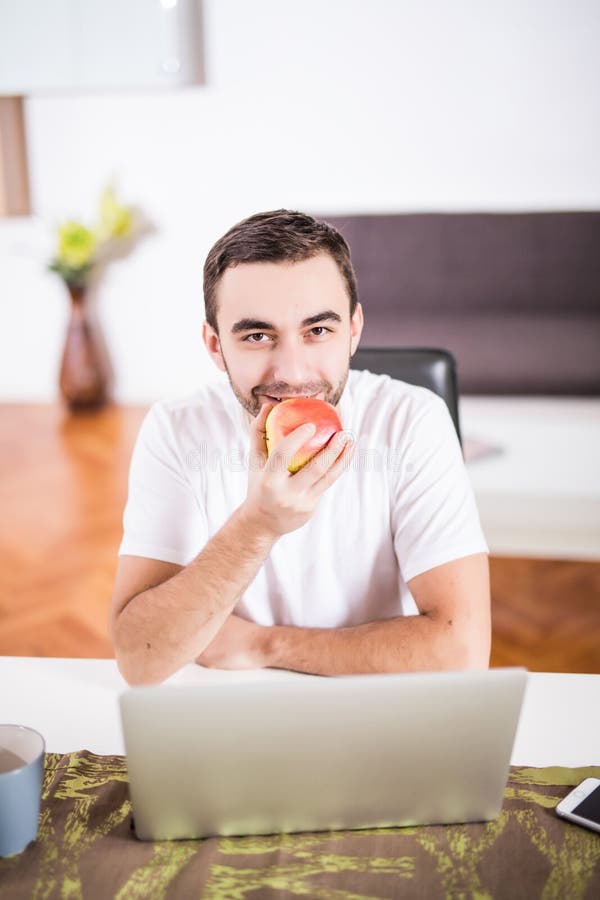 Handsome Man Eating Apple and Working with Laptop at Kitchen at Home ...
