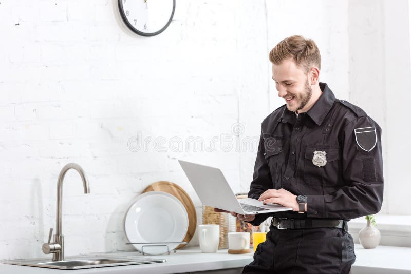 Handsome Man In Police Uniform Smiling And Using Laptop Stock Photo ...