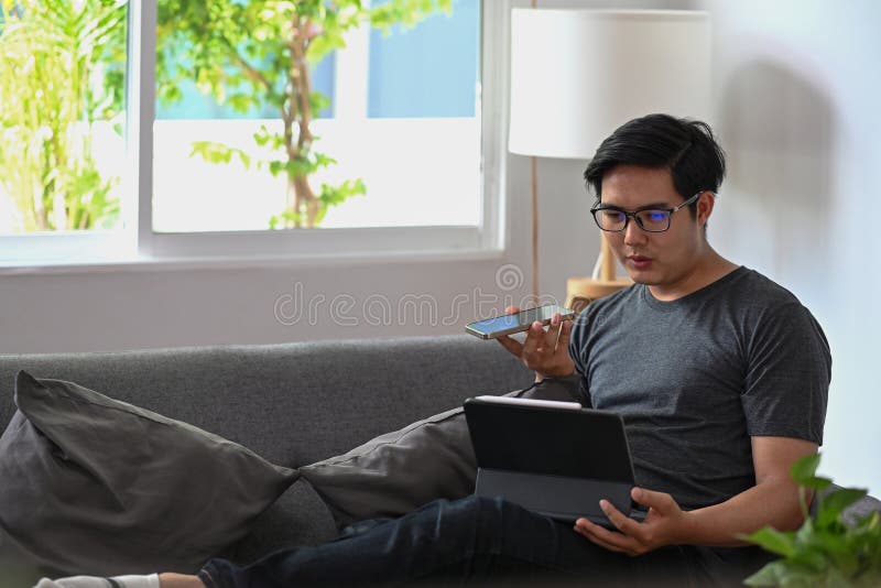 Man Talking on Speaker Phone and Using Computer Tablet on Sofa. Stock ...
