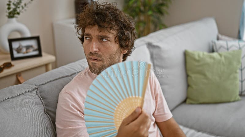 Handsome Man Using Fan while Sitting on Couch Indoors, Looking Tired ...