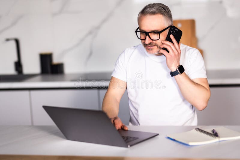Handsome Mature Man Talking on Mobile Phone while Using Laptop at the ...