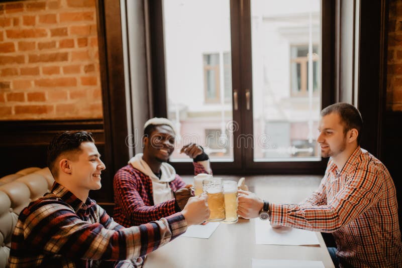 Handsome Multiethnic Men are Clinking Cup of Beer Talking Smiling while ...