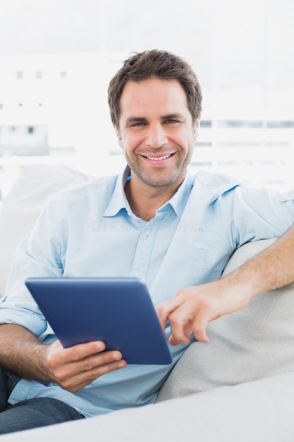 Handsome Smiling Man Sitting on the Sofa Using His Tablet Pc Stock ...