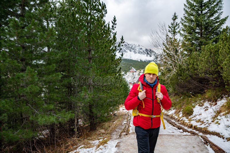A Handsome Tourist in a Red Down Jacket, Yellow Hat and Backpack Stands ...