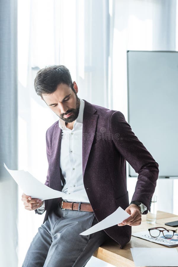 Handsome Young Businessman Doing Paperwork while Leaning Back on Desk ...