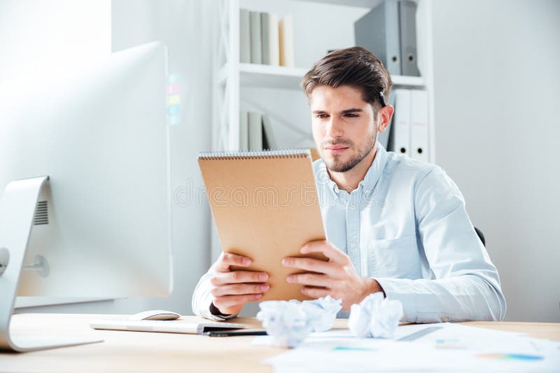 Handsome Young Businessman Man Sitting and Reading Notes in Notebook ...