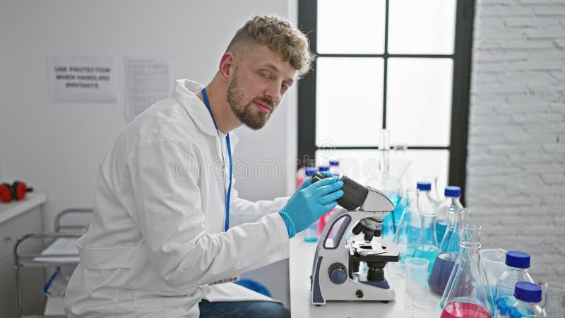 Handsome Young Man with a Beard Examines Samples Under a Microscope in ...