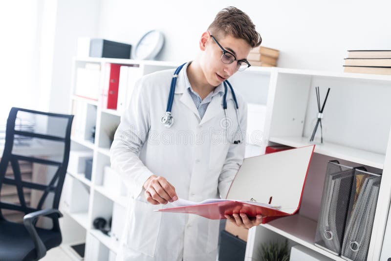 A Young Doctor in a White Robe Standing Near the Rack and Holding a ...