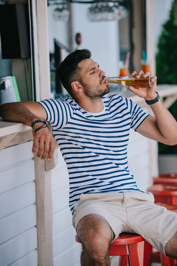 Handsome Young Man Drinking Beer from Glass Bottle while Sitting at ...