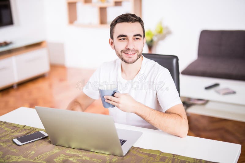 Handsome Young Man Drinking Coffee while Working with Laptop in Kitchen ...