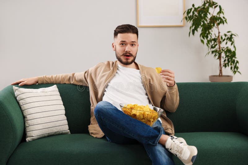 Handsome Young Man Eating Tasty Potato Chips on Sofa at Home Stock ...