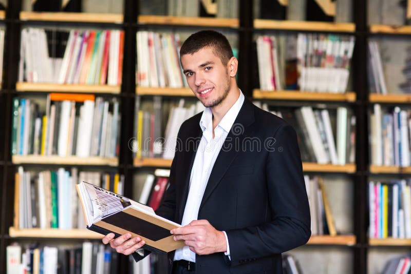 Handsome Young Man Holding Books and Smiling while Standing in Library ...
