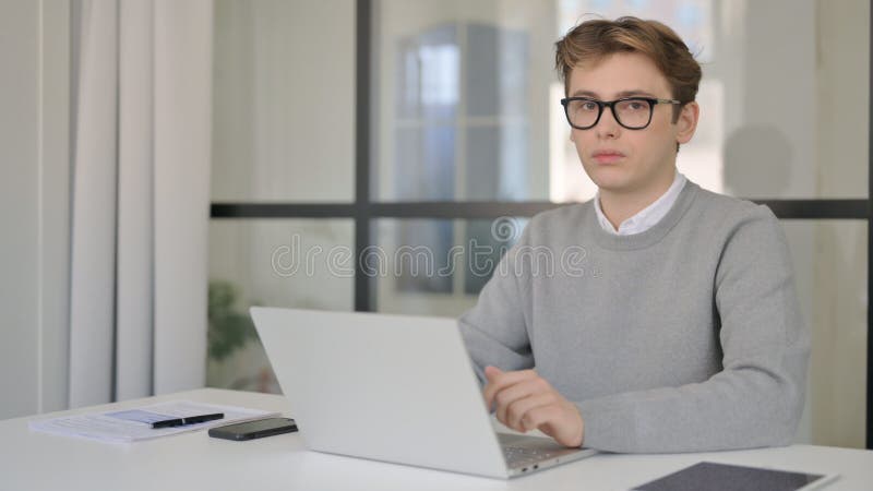 Young Man Looking at Camera while Using Laptop in Modern Office Stock ...
