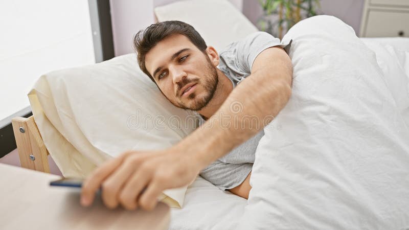 Handsome Young Man Lying in Bed Reaching for Something in Bright ...