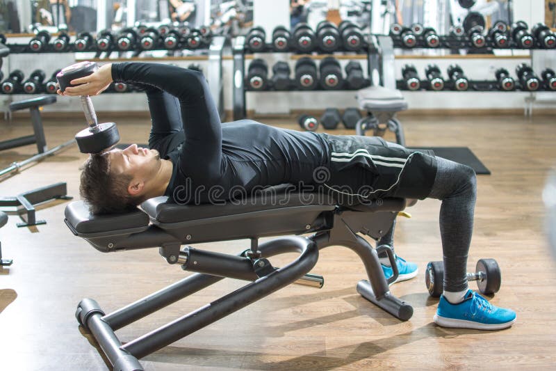 Handsome Young Man Lying on Exercise Bench and Lifting Dumbbell in Gym ...