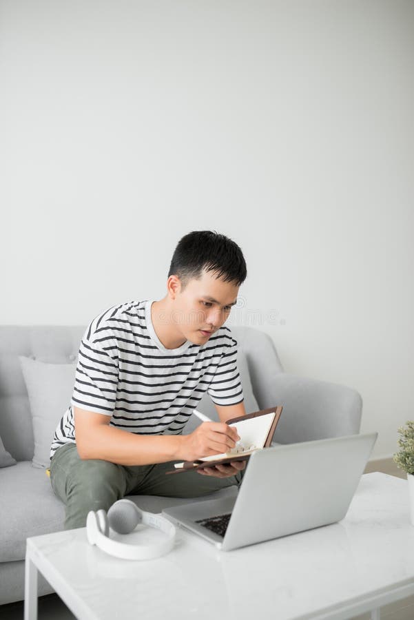 Handsome Young Man Sitting on the Living Room Couch, Writing Some Notes ...