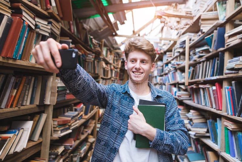 Handsome Young Man Standing in a Library with Books in His Hands and ...