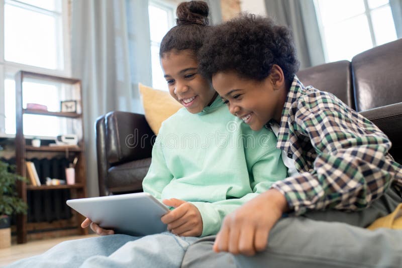 Happy Affectionate Siblings Watching Video On The Floor By Couch In
