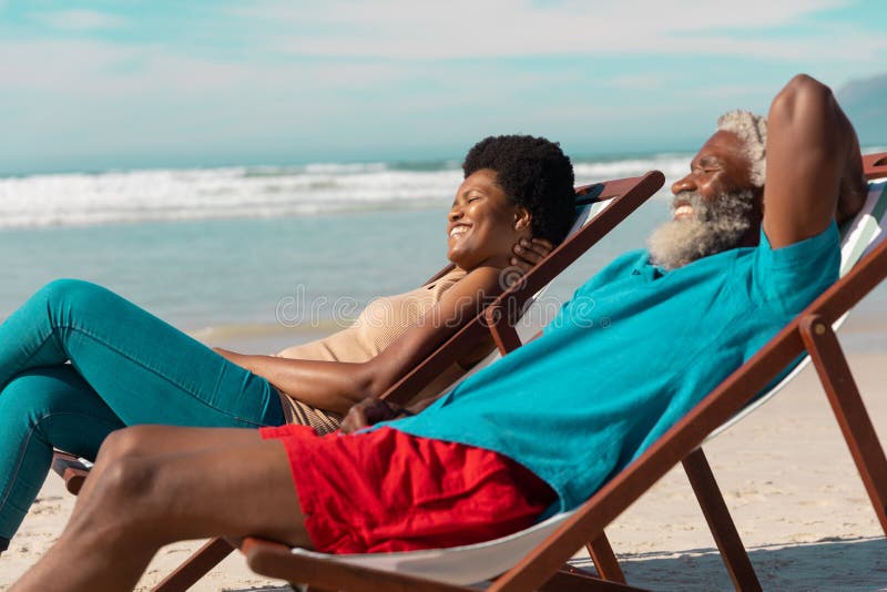 Happy African American Couple Relaxing On Deckchairs Against Sea And