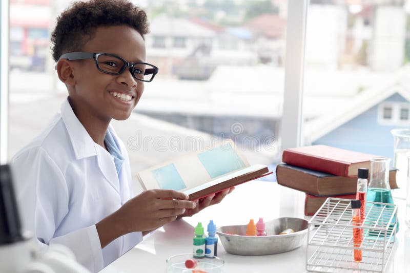 Happy African Boy in Lab Coat Reading a Textbook before Doing Science ...