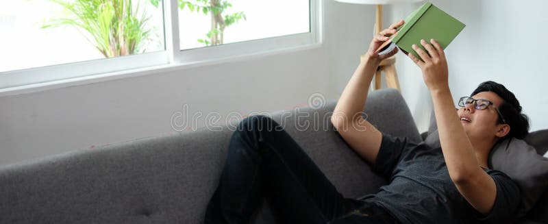 Happy Asian Man Lying on Couch and Reading a Book Stock Image - Image ...