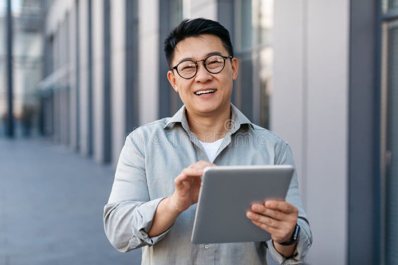 Happy Asian Middle Aged Businessman Using Tablet, Looking and Smiling ... Happy Asian Middle Aged Businessman Using Tablet, Looking and Smiling ...