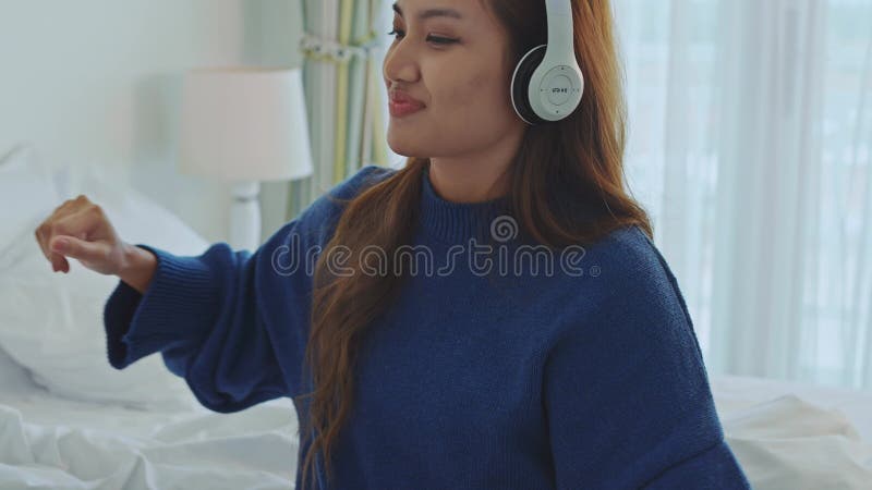 Happy Asian Woman Dancing And Listening To Music With Headphones On Bed