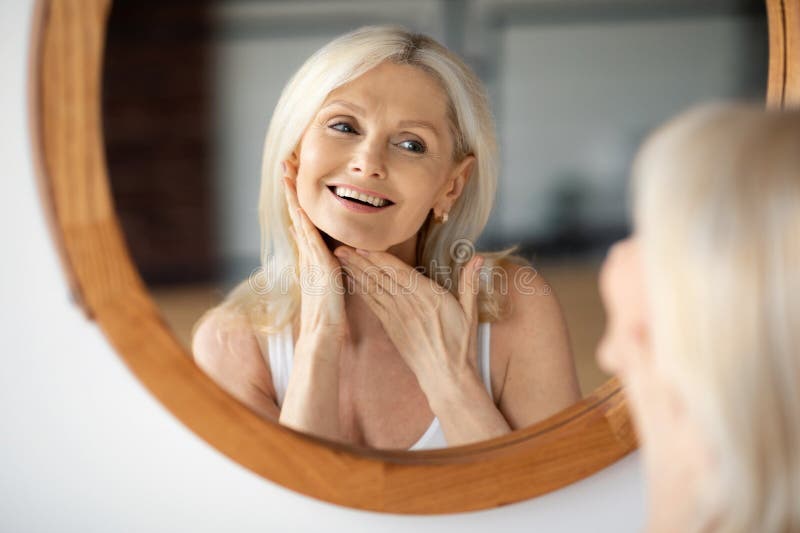 Happy Attractive Senior Woman Looking At Mirror And Touching Her Soft