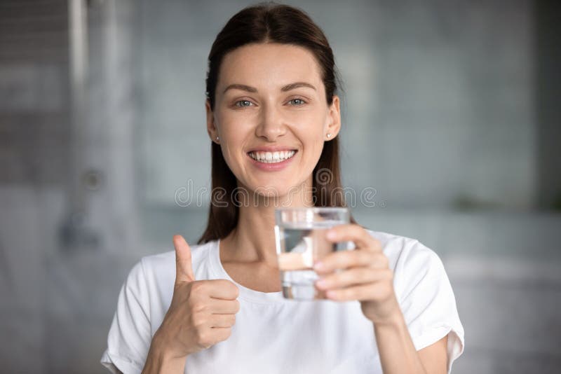 Happy Attractive Woman Holding Glass Of Water Showing Thumbs Up Stock