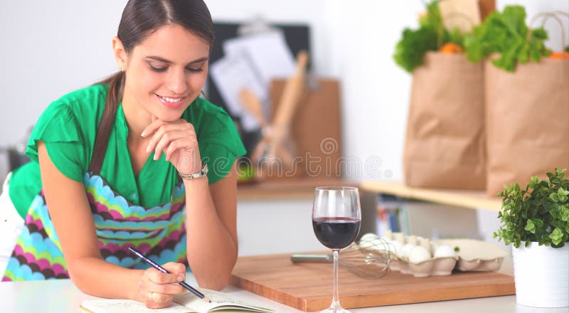 Happy Beautiful Woman Standing in Her Kitchen Writing on a Notebook at ...
