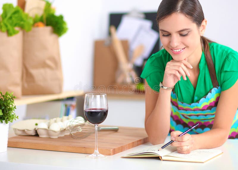 Happy Beautiful Woman Standing in Her Kitchen Writing on a Notebook at ...