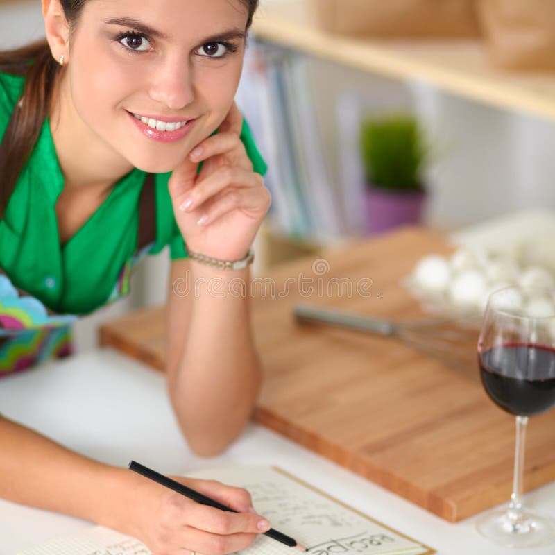 Happy Beautiful Woman Standing in Her Kitchen Writing on a Notebook at ...