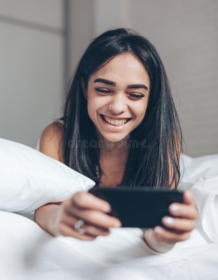 Happy Beautiful Woman Texting At Smartphone While Lying On Her Bed