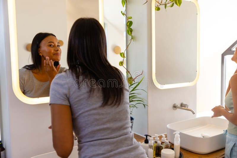 Happy Biracial Lesbian Couple Looking In Mirrors In Bathroom Stock