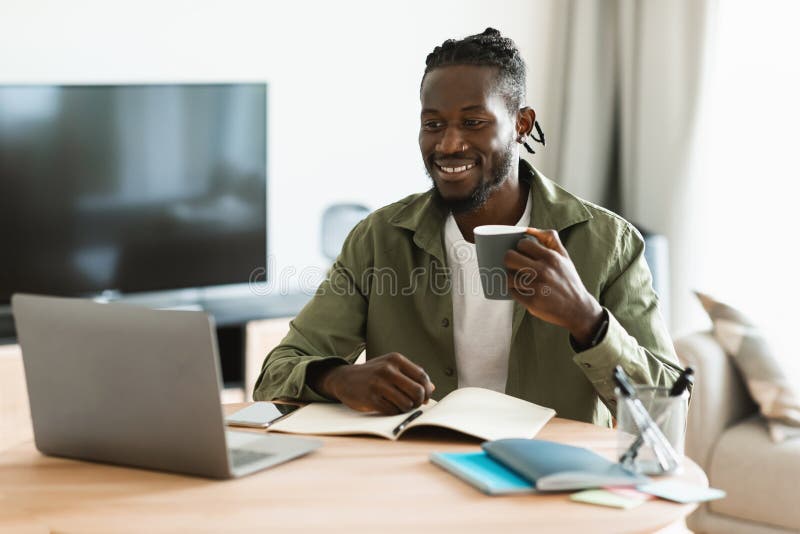 Happy Black Man Drinking Cup of Tea at Workplace while Working on ...