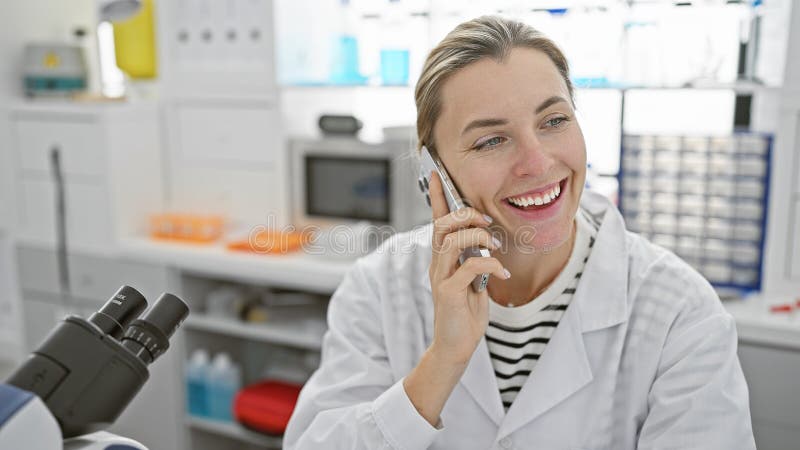 Happy Blonde Woman in White Lab Coat Talking on Phone in a Laboratory ...