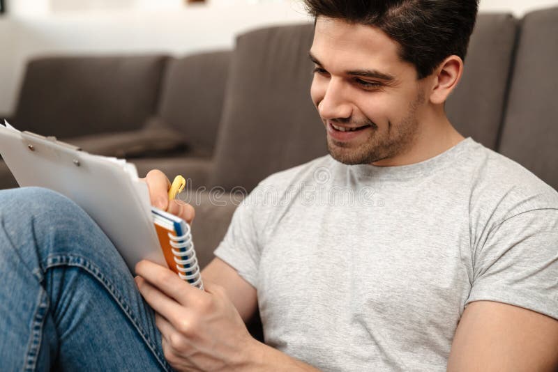 Happy Brunette Guy Writing Down Notes while Sitting on Floor Stock ...