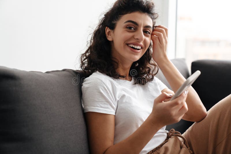 Happy Brunette Young Woman Using Mobile Phone while Sitting on Sofa ...
