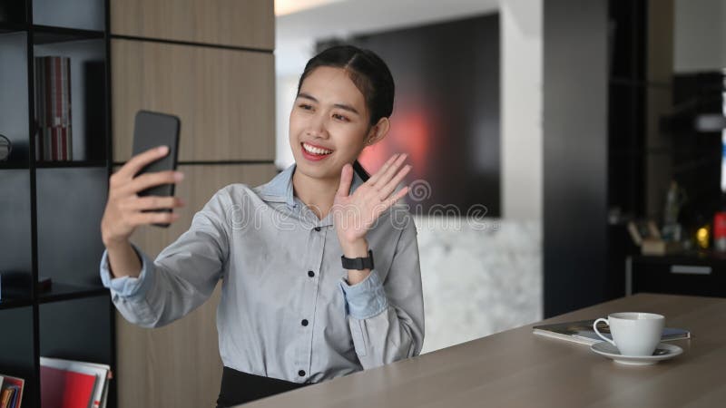 Businesswoman Smiling and Making Video Call Via Mobile Phone at Office ... Businesswoman Smiling and Making Video Call Via Mobile Phone at Office ...