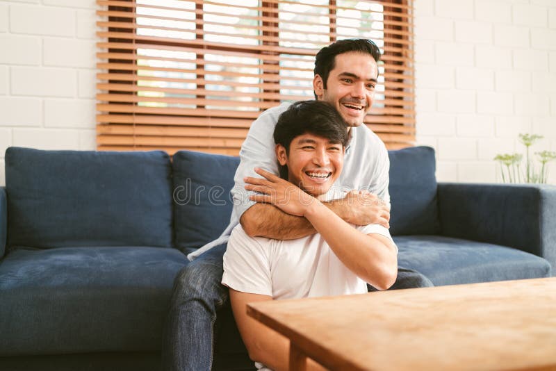 Happy Caucasian And Asian Lgbt Couple One Sitting On The Sofa