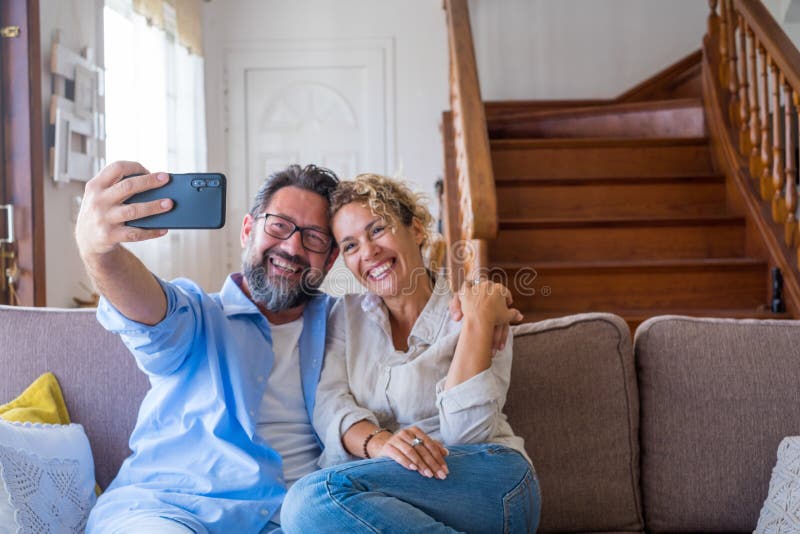 Happy Caucasian Couple Taking Selfie Sitting On Sofa Using Mobile Phone