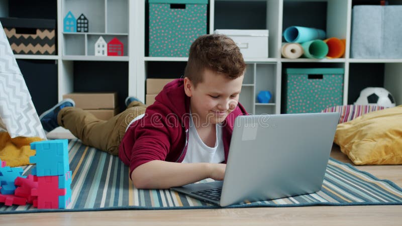 Happy Child Using Laptop Computer Typing and Smiling Lying on Floor at ...