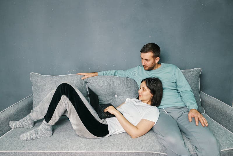Happy Couple Embracing Using Laptop Together Relaxing On Sofa At Home