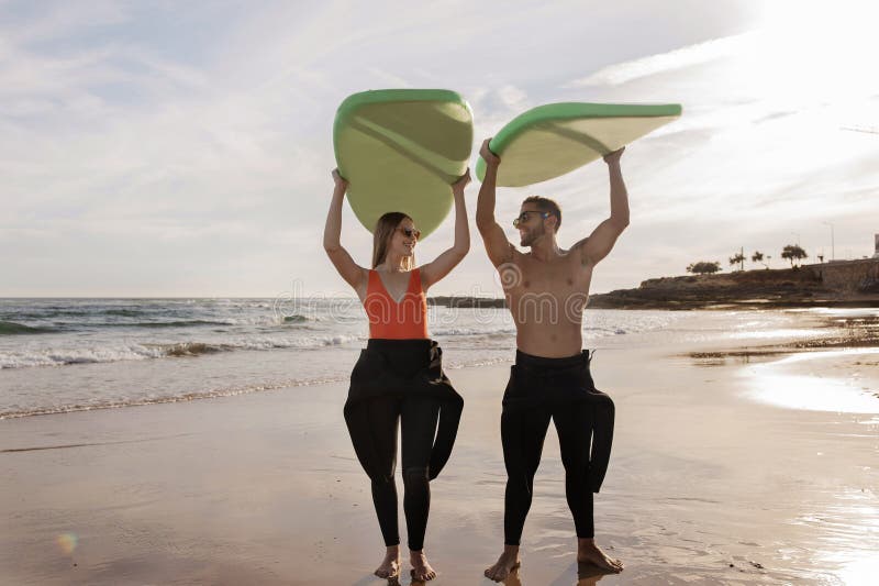Happy Couple Having Fun On The Beach Holding Surfboards Above Their