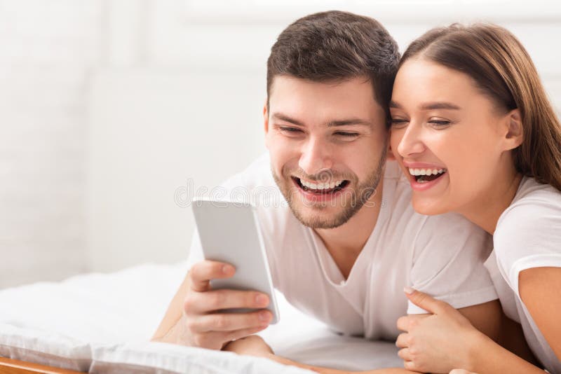 Happy Couple Using Smartphone Texting Lying in Bed in Bedroom Stock ...
