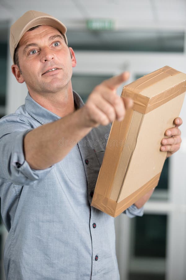 Happy Delivery Man Holding Gift Pack while Pointing at Something Stock ...