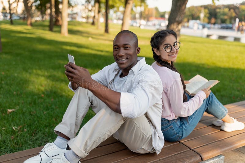 Happy Diverse College Students Sitting Back To Back, Using Smartphone ...
