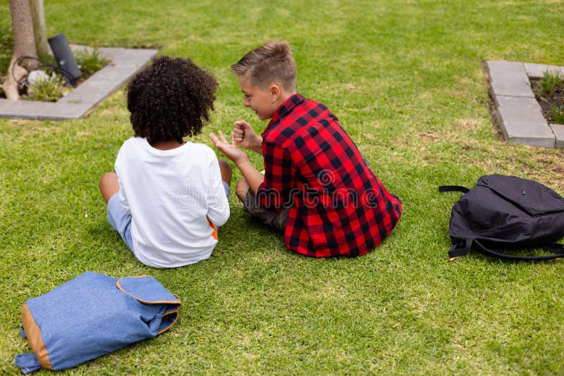 Happy Diverse Schoolchildren Talking and Sitting on Grass at School ...