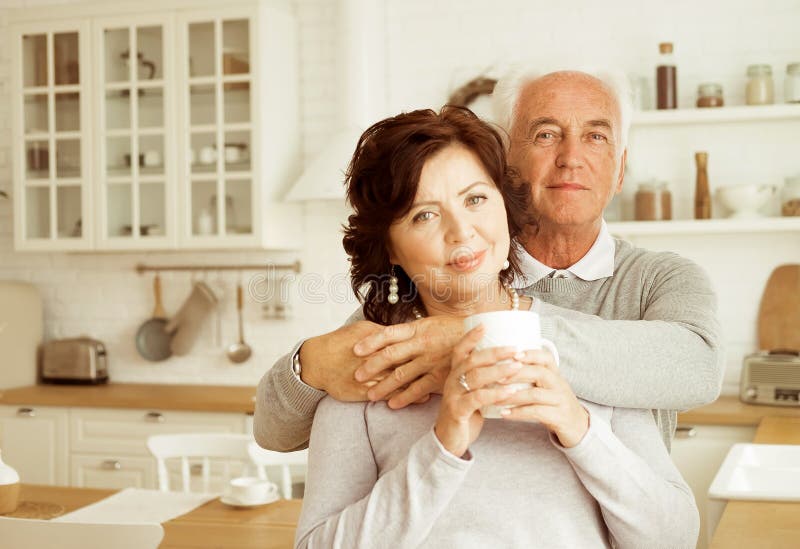 Happy Elderly Couple Hugging In The Kitchen At Home Love And Trust
