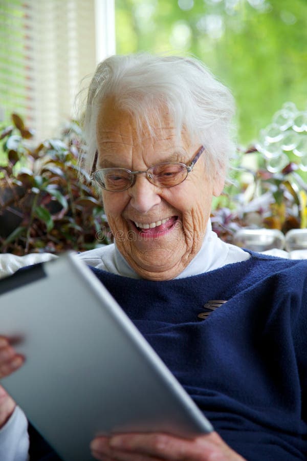 Happy Elderly Woman Using a Tablet Looking at the Camera and Laughing ...